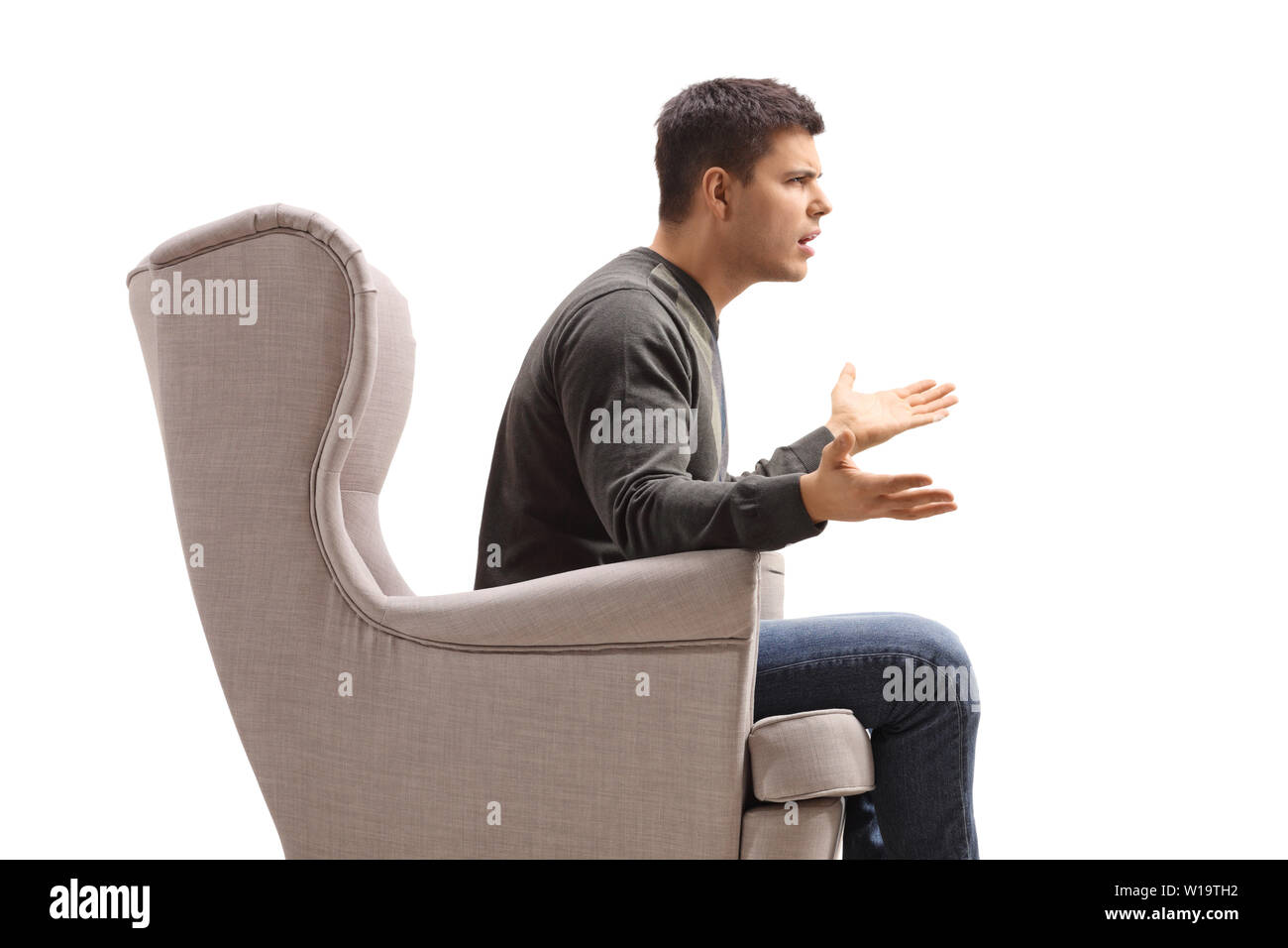 Profile of a young man sitting in an armchair and arguing with someone ...
