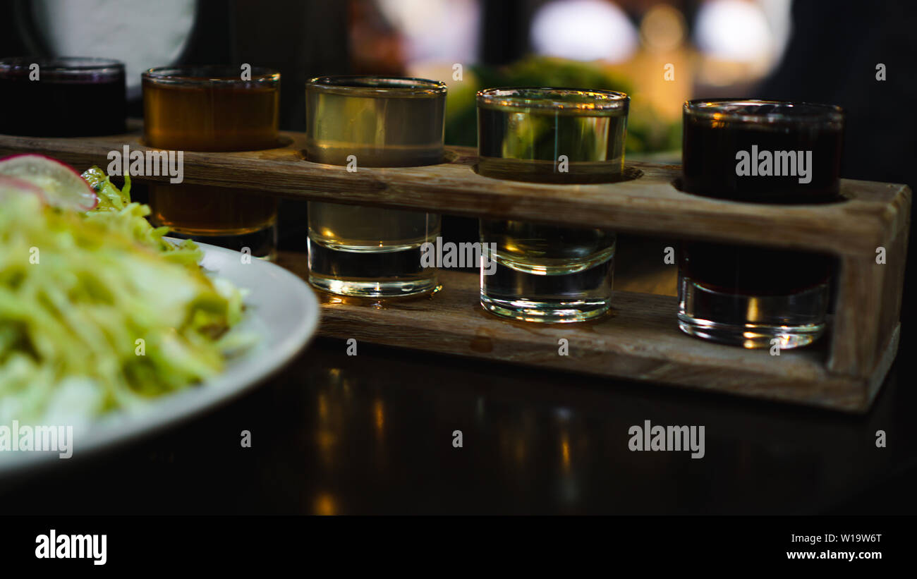 Set of shots in one row, six servings on a wooden stand and grren salad ...
