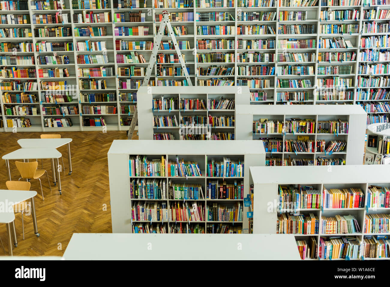 racks with collection of books near wooden desks and chairs in library ...
