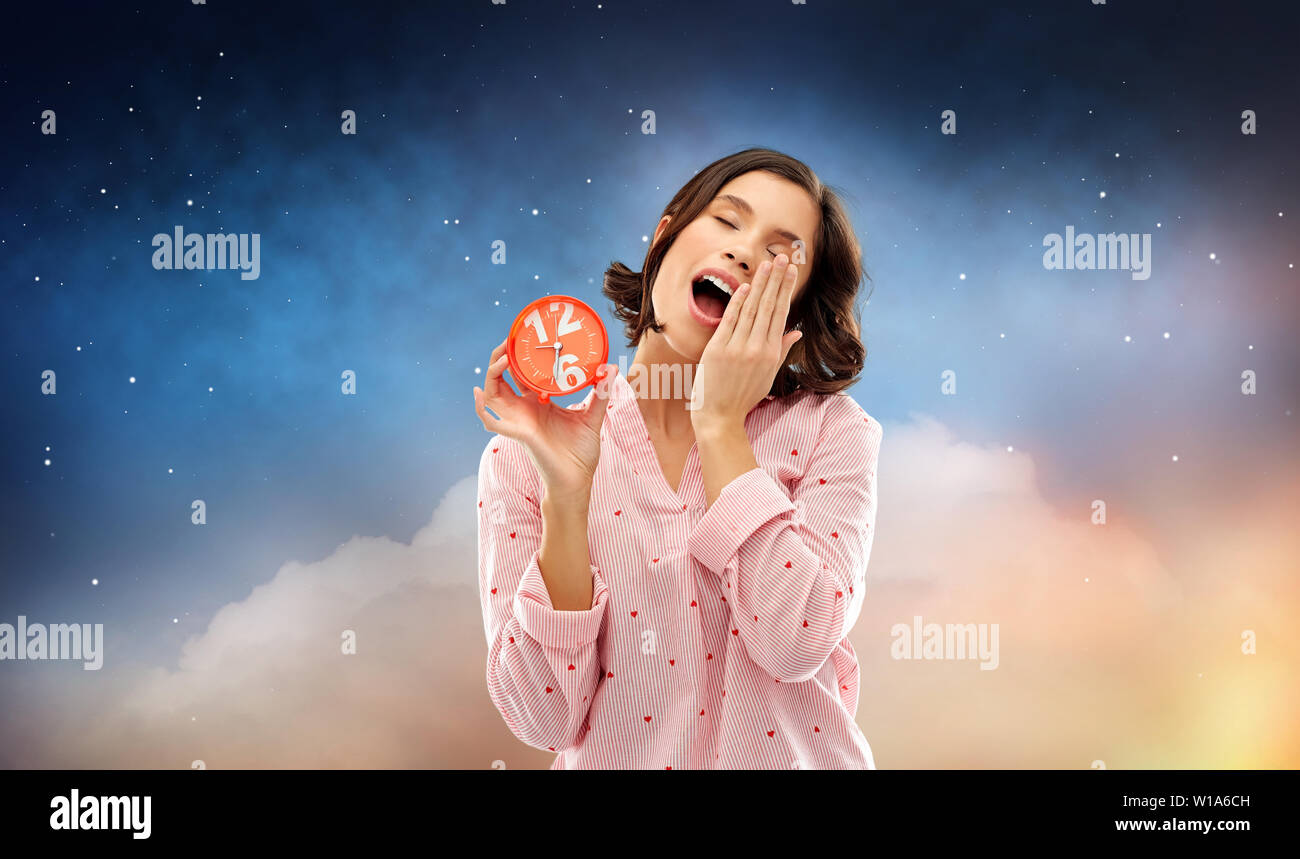 sleepy woman in pajama with alarm clock yawning Stock Photo - Alamy