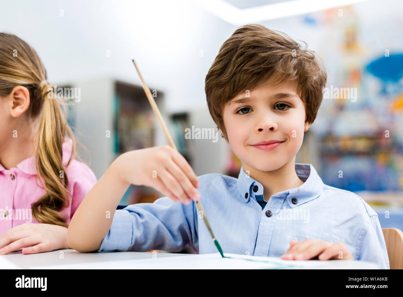happy kid holding paintbrush near child and looking at camera Stock ...