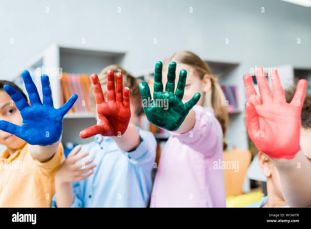 selective focus of multicultural kids covering faces with colorful ...