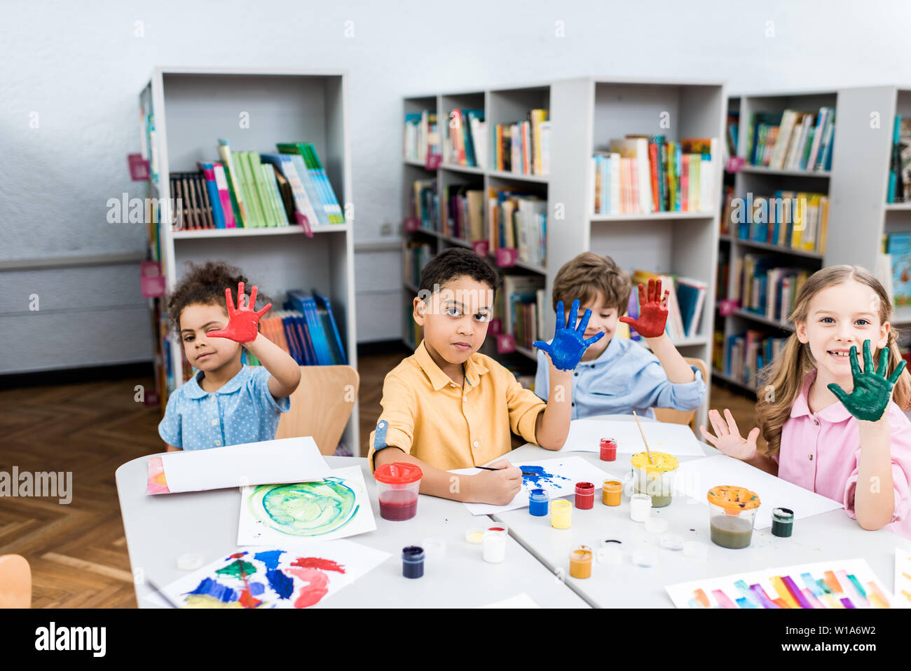cheerful multicultural kids showing colorful hands with gouache paint ...