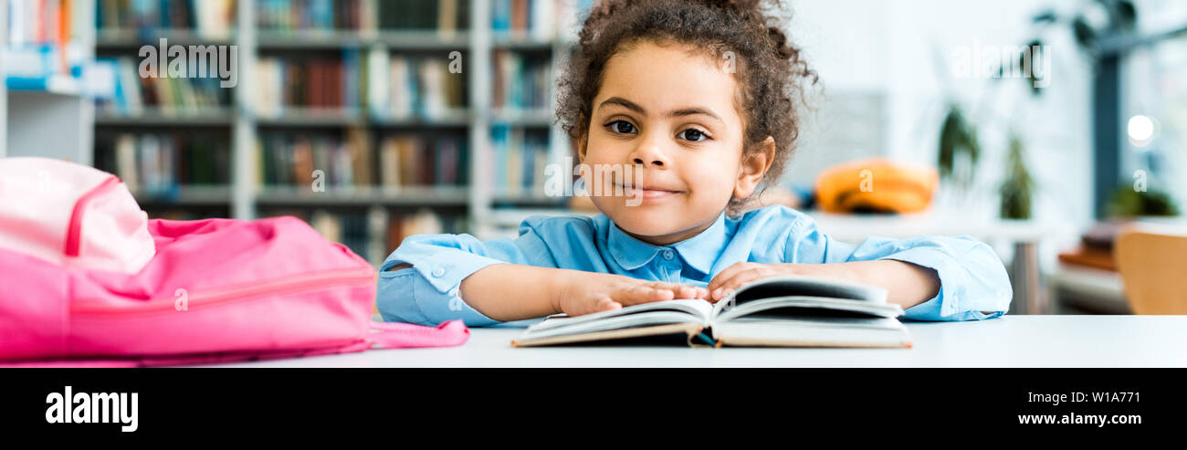 panoramic shot of happy african american kid sitting near book in ...