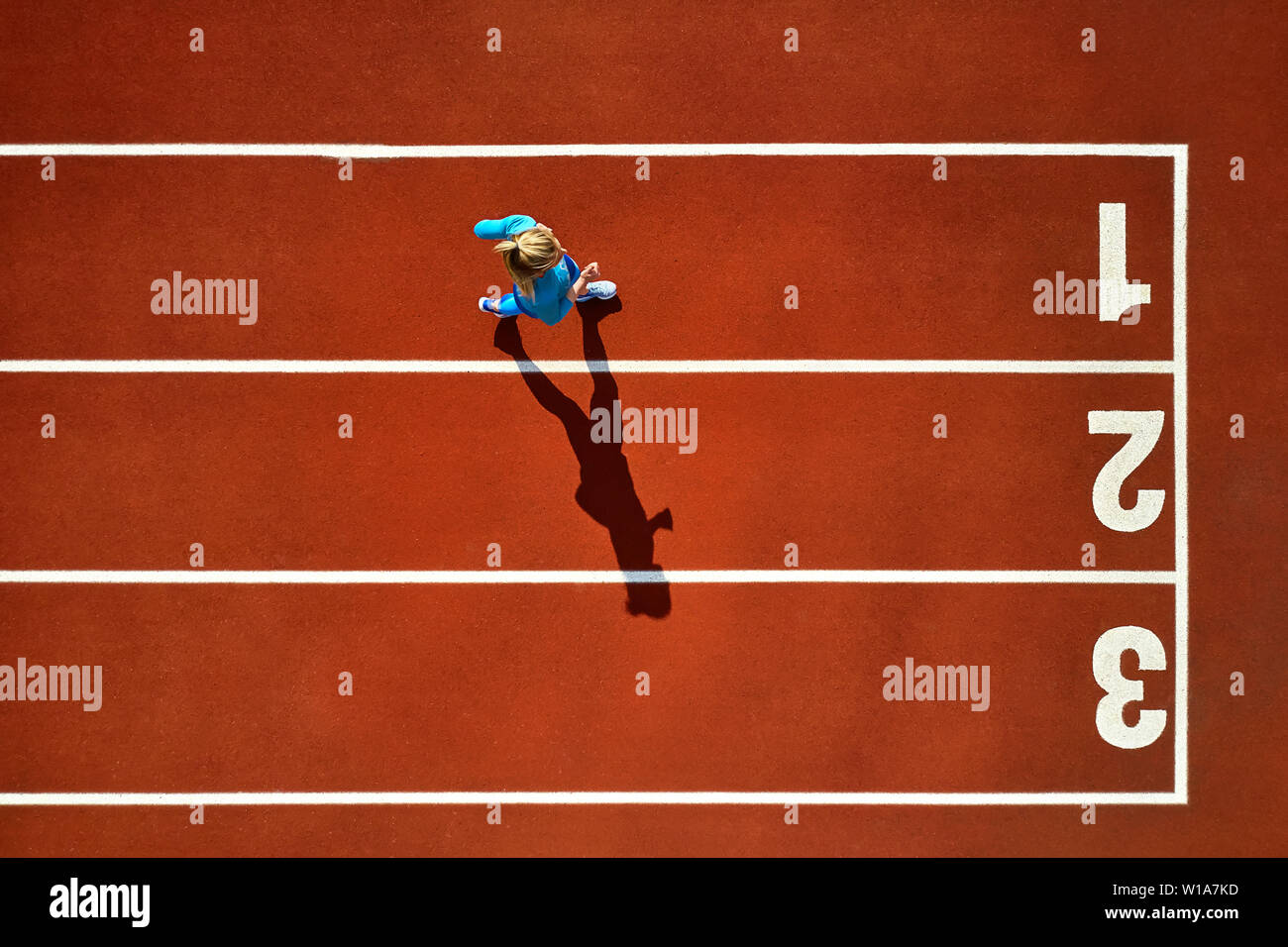 Cute girl in a blue sportswear and sneakers runs on the running track ...