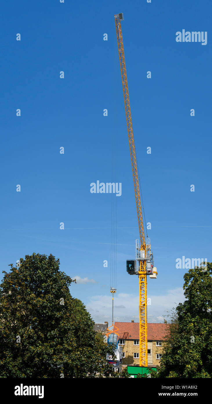 Tall yellow tower crane lifting & working on construction site against ...