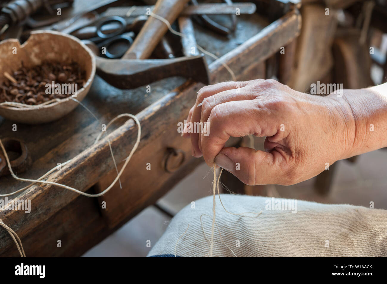 Shoemaker prepares the string for sewing a shoe. Various tools and ...