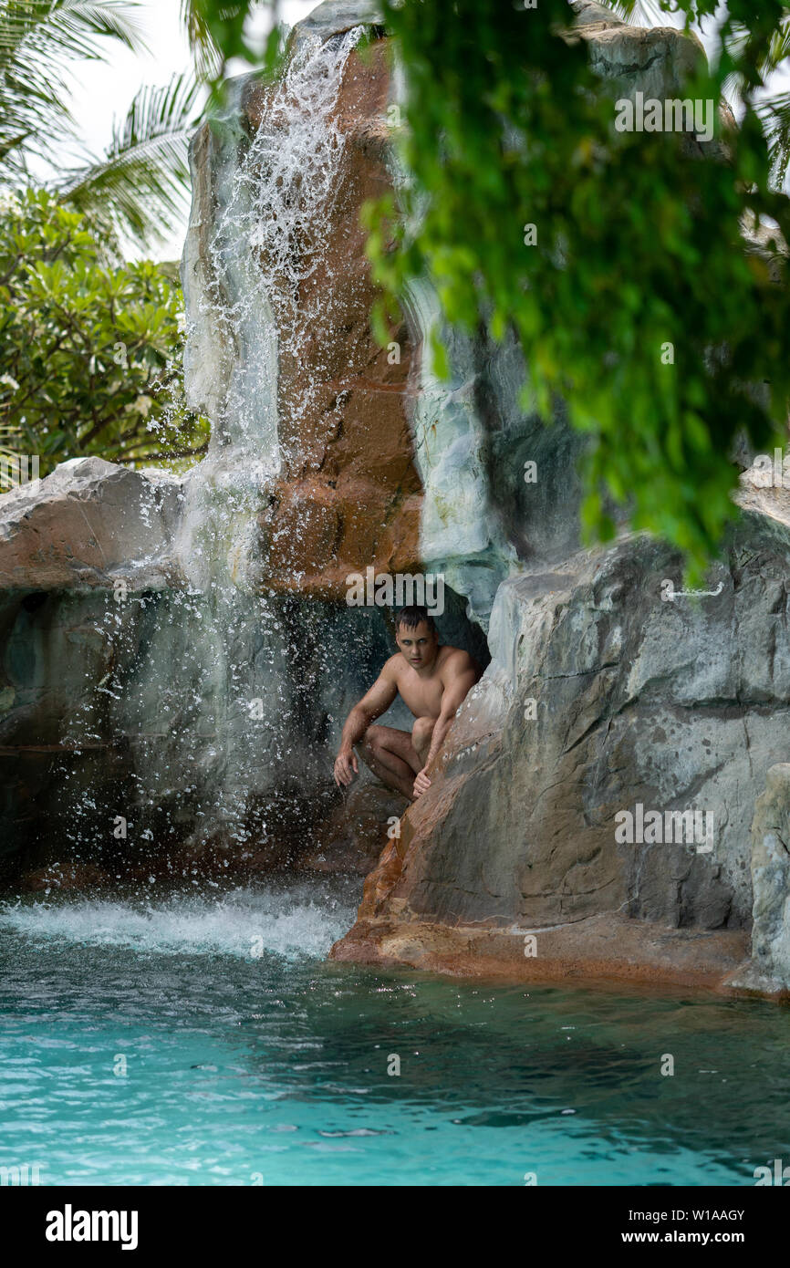 A young guy sits in a rock behind a waterfall Stock Photo - Alamy