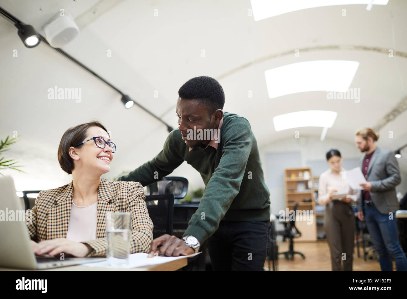 Portrait of young African businessman smiling at female colleague while ...
