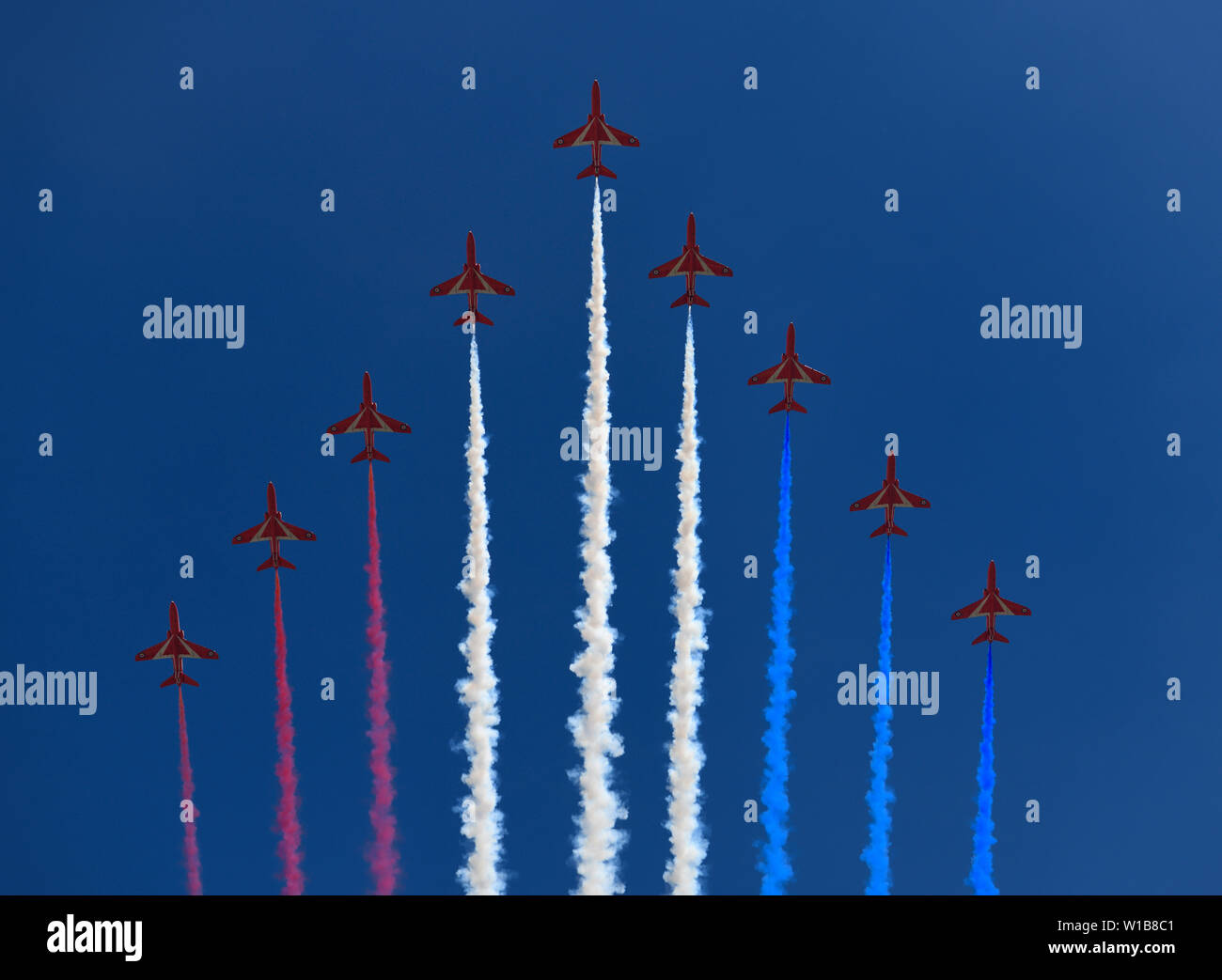 Formation of RAF Red Arrows with coloured trails on blue sky for ...