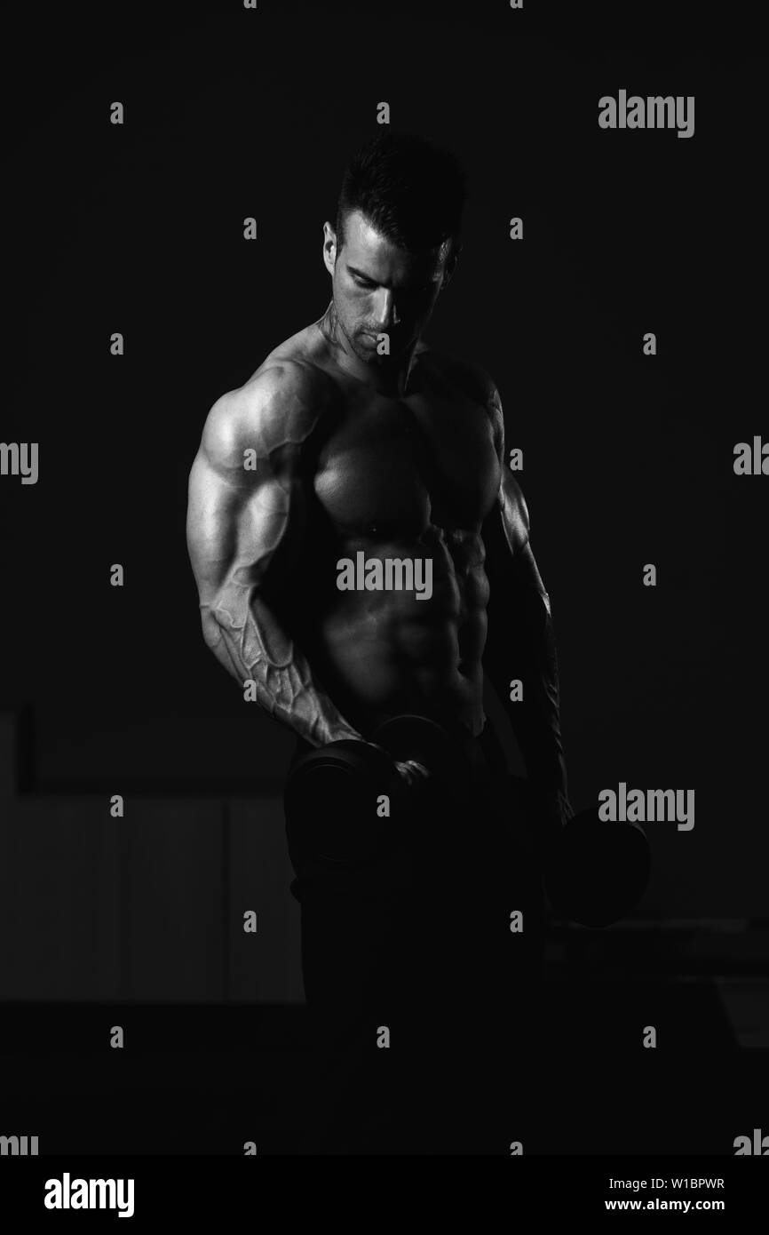 Healthy Man Working Out Biceps In A Dark Gym - Dumbbell Concentration ...