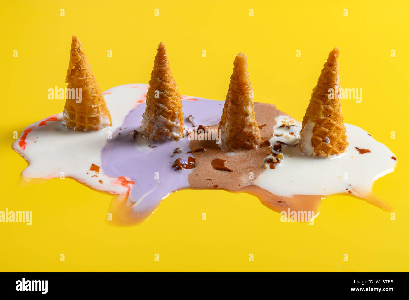 side view multiple flavor ice cream cones melted on yellow background ...