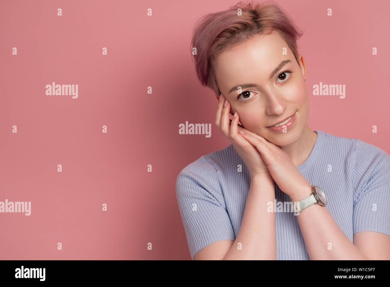 Pink-haired young woman looks at the camera with quiet smile putting ...
