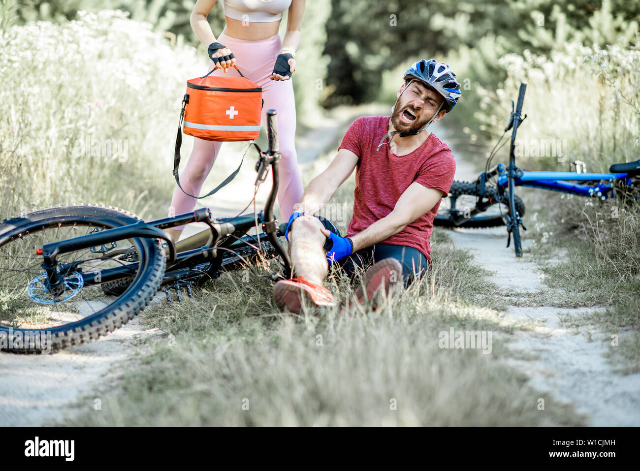 Woman giving first aid to a man with knee injury while cycling on the ...