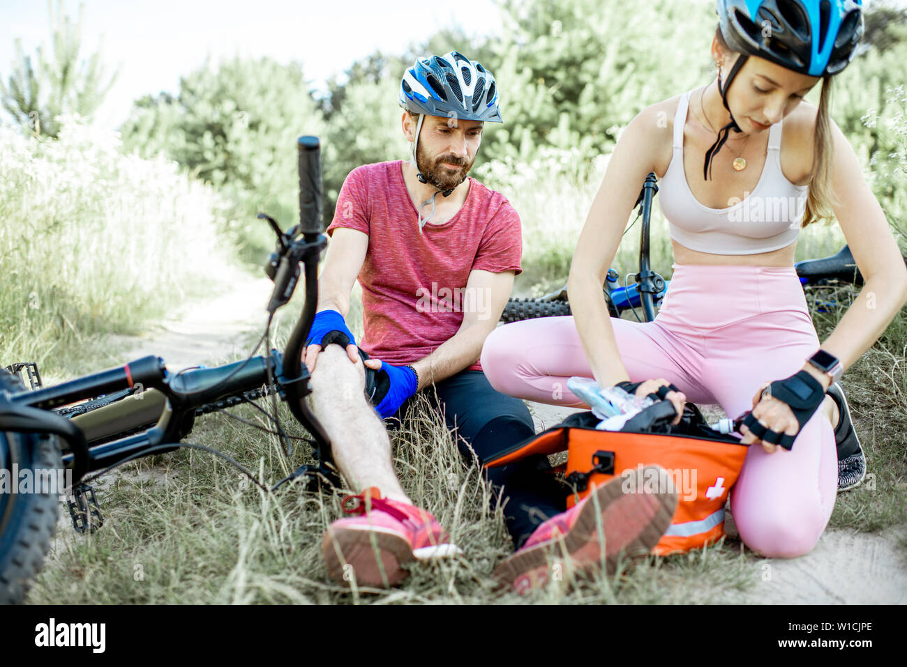 Woman giving first aid to a man with knee injury while cycling on the ...