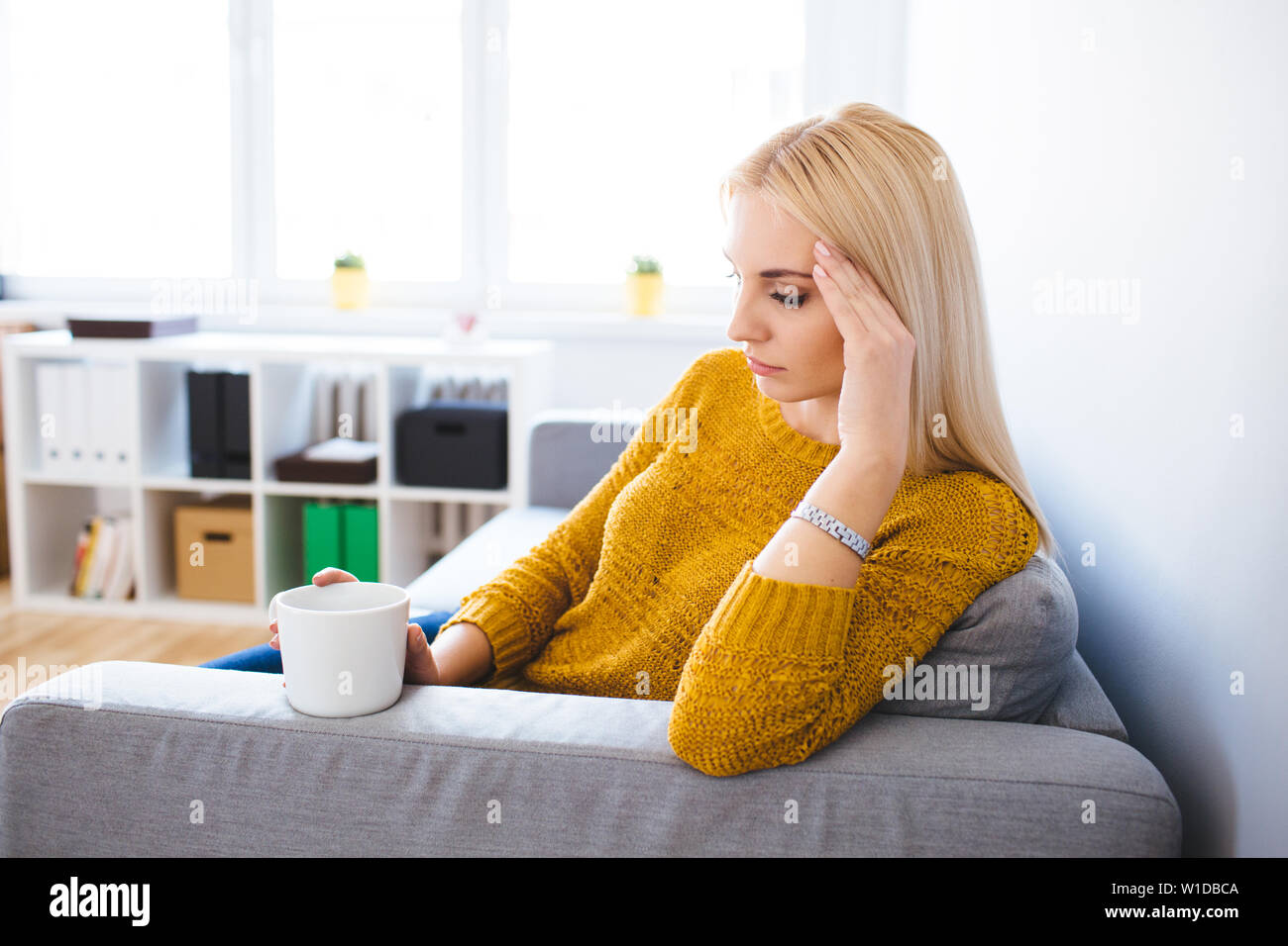 Depressed young woman sitting with cup of coffee in living room Stock ...