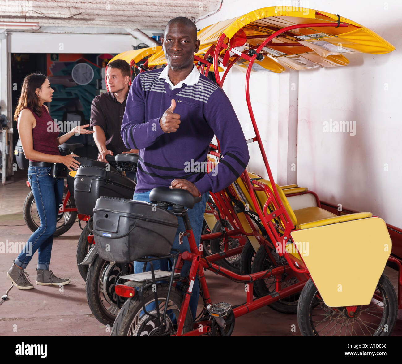 Positive African-American man pedicab driver standing near rickshaw ...
