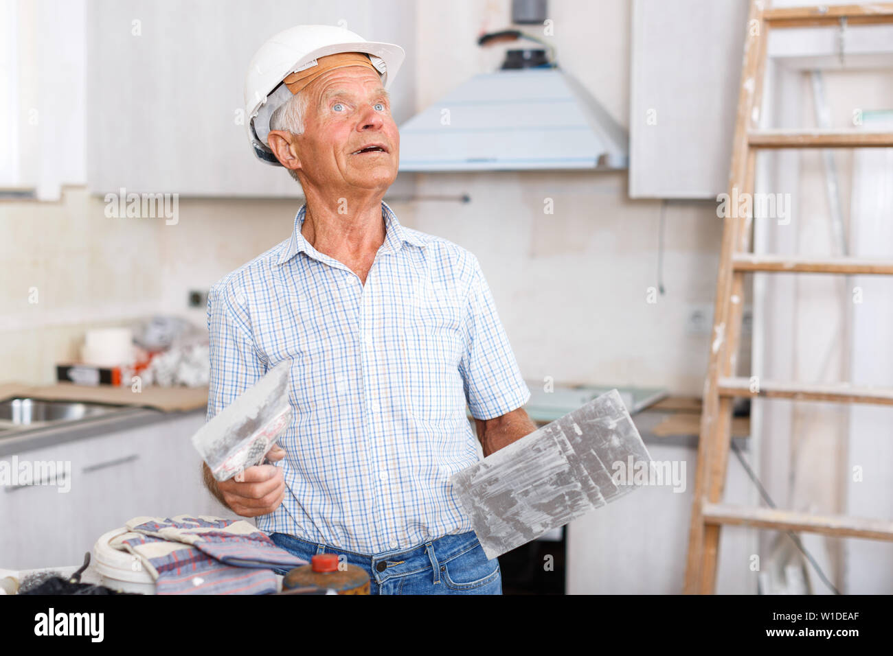 Puzzled aged worker in hardhat working on house overhaul, checking ...