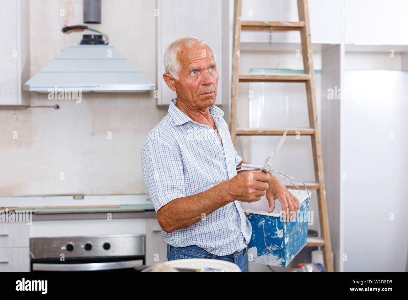 House renovation, elderly man renovating indoor walls with spatula and ...