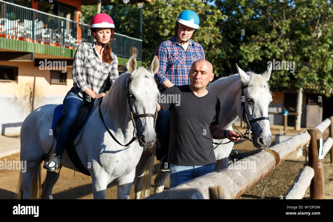 Positive mature couple with jockey learn to riding horse at farm ...