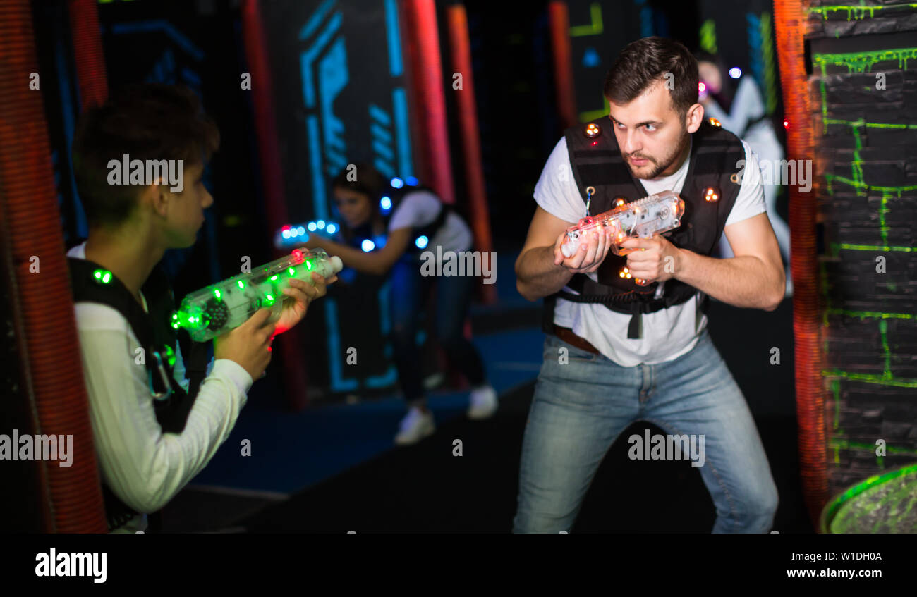 Emotional guy with laser pistol playing laser tag with friends on dark ...