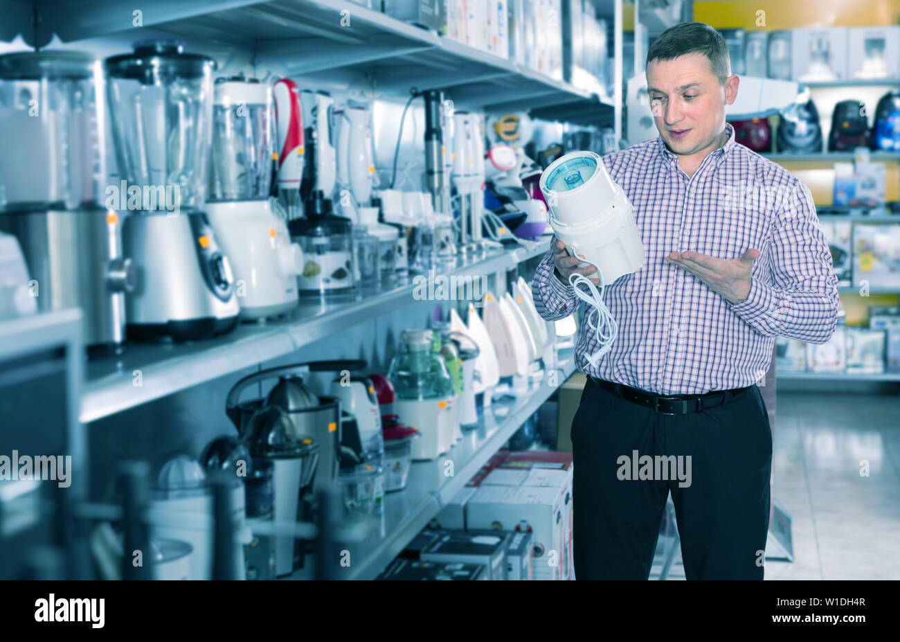 Positive man is choosing blender for his kitchen in appliances shop ...