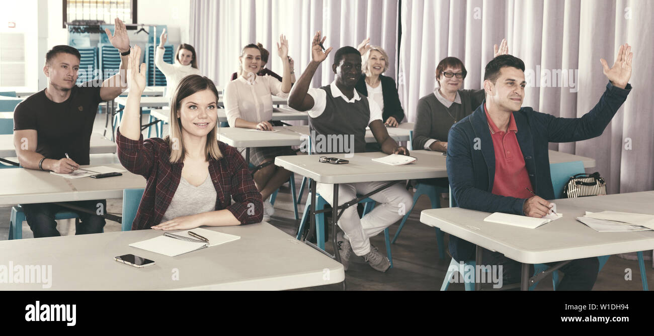 Group of adult people studying together in classroom, raising hands to ...
