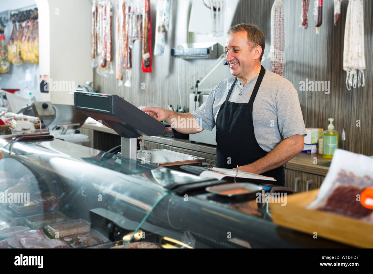 Mature male butcher with eco wurst and smoked meat at counter Stock ...