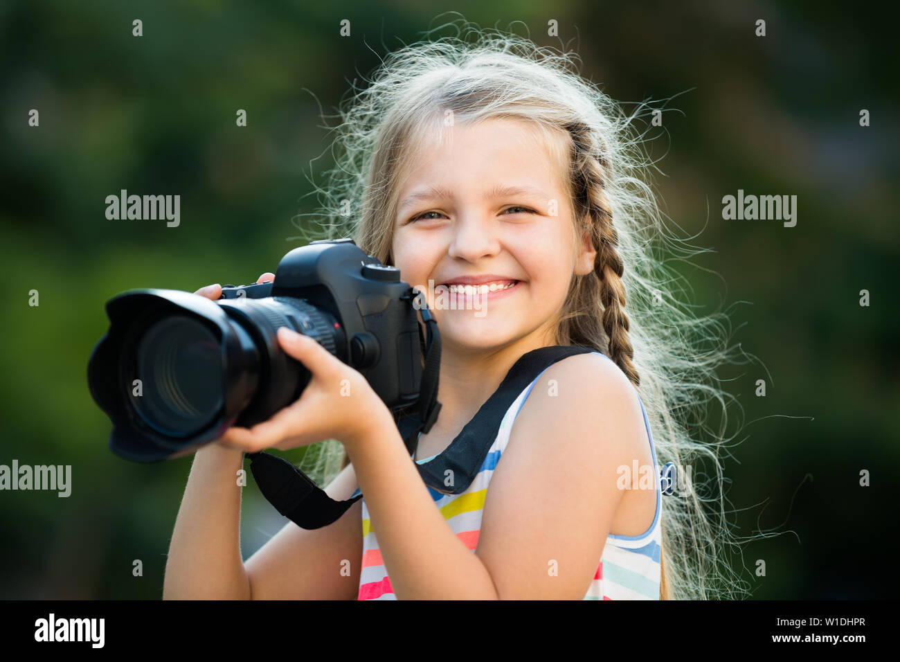 positive female child taking pictures with camera in park on summer day ...