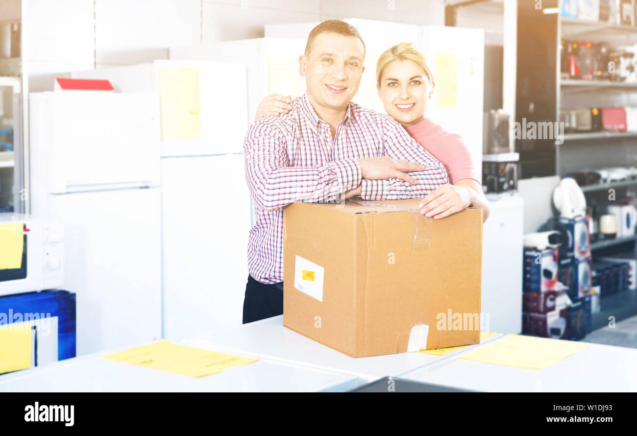 Positive smiling couple with packed purchases in household appliances ...