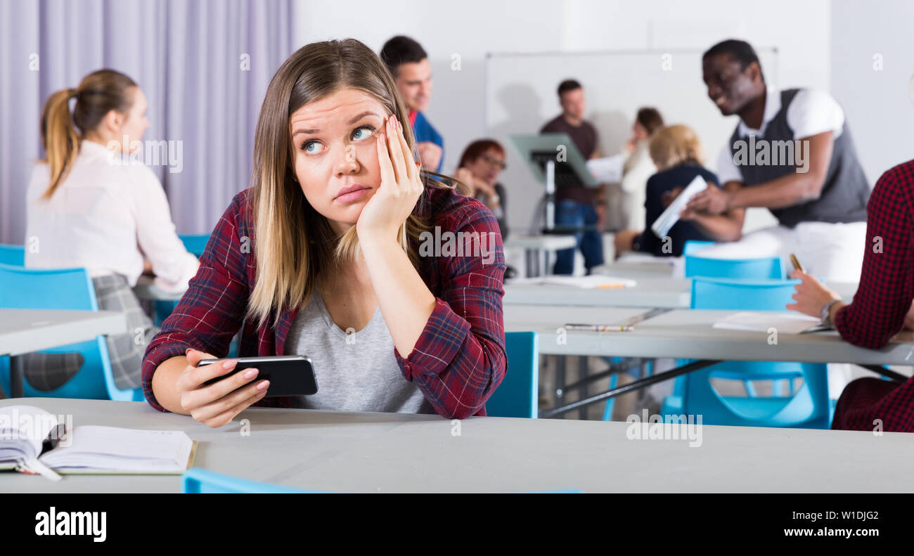 Frustrated young woman student sitting with phone in classroom in break ...