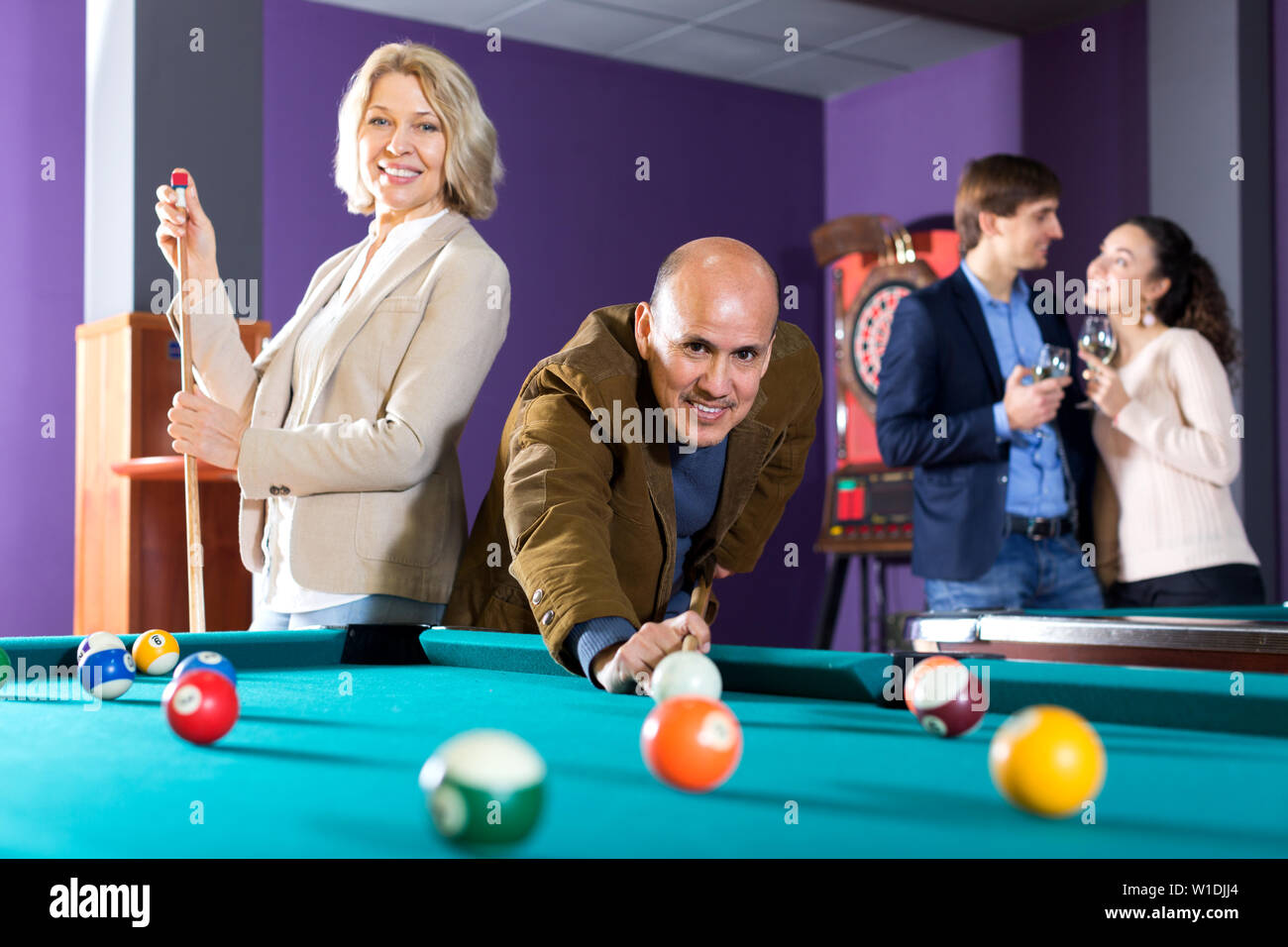 Positive group of friends playing billiards and smiling in billiard ...