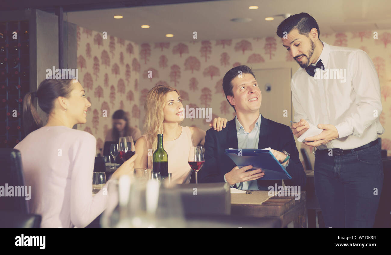 Glad waiter helping group of friends with menu, taking order in ...