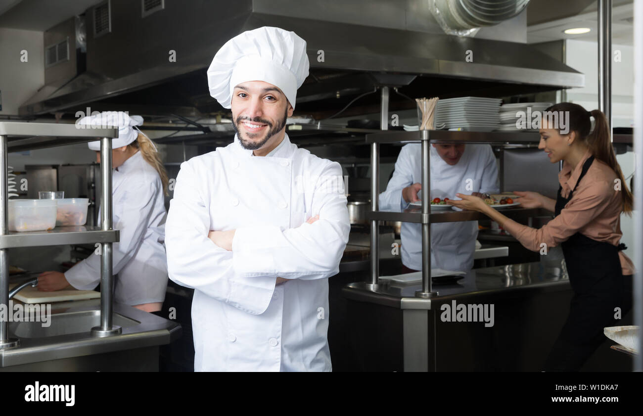 Positive chef of restaurant posing in kitchen on background with ...