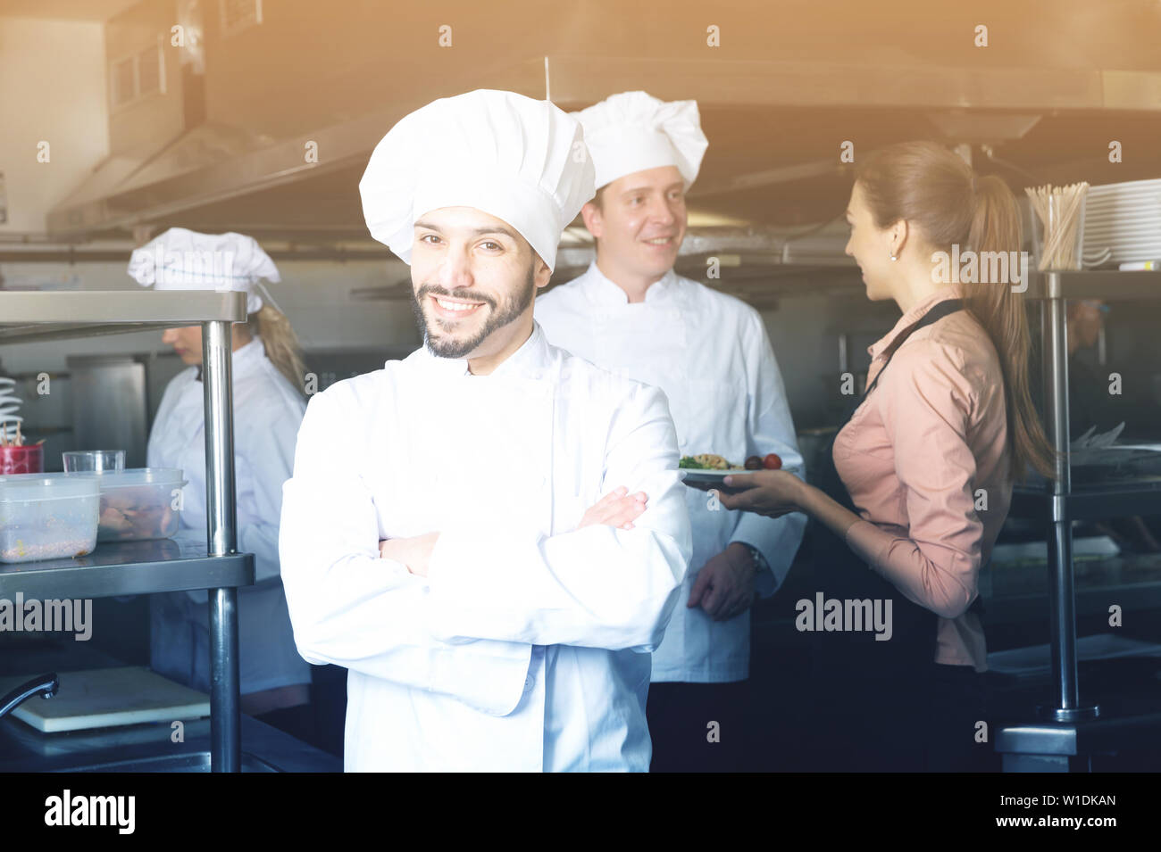 Portrait of satisfied smiling chef on restaurant kitchen with busy ...