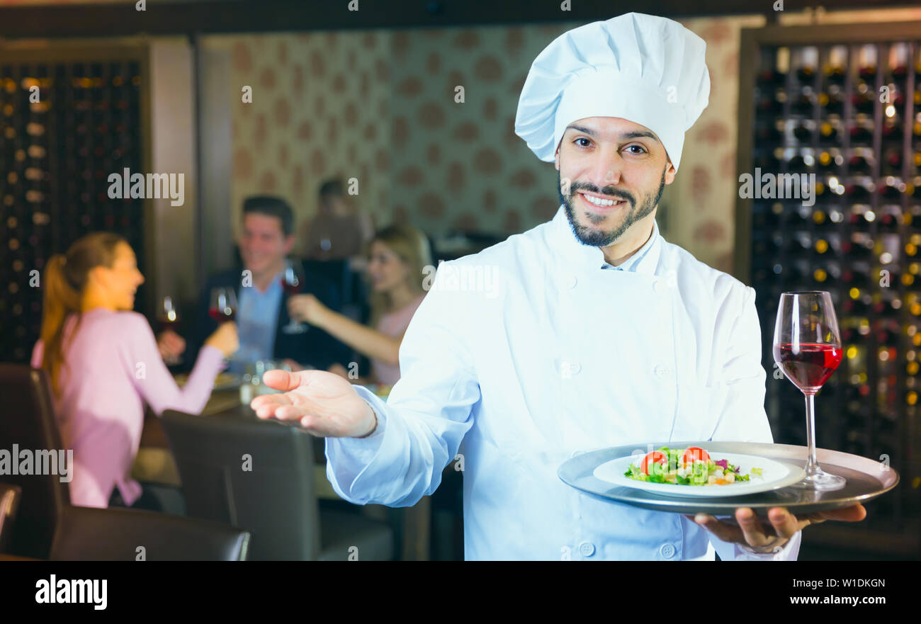 Portrait of young professional chef with serving tray meeting ...