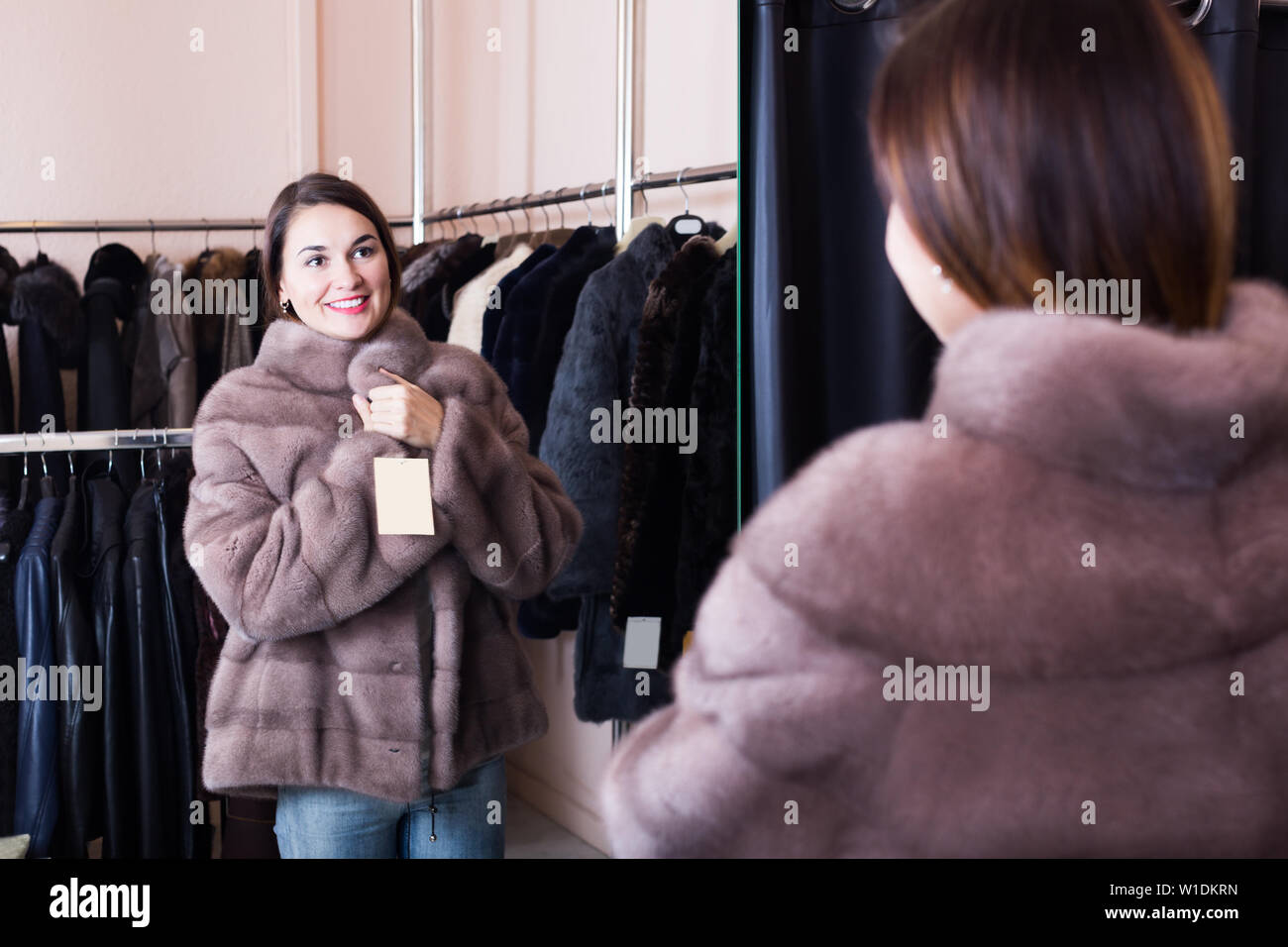 Smiling girl customer examining mink fur coat in women’s cloths shop ...