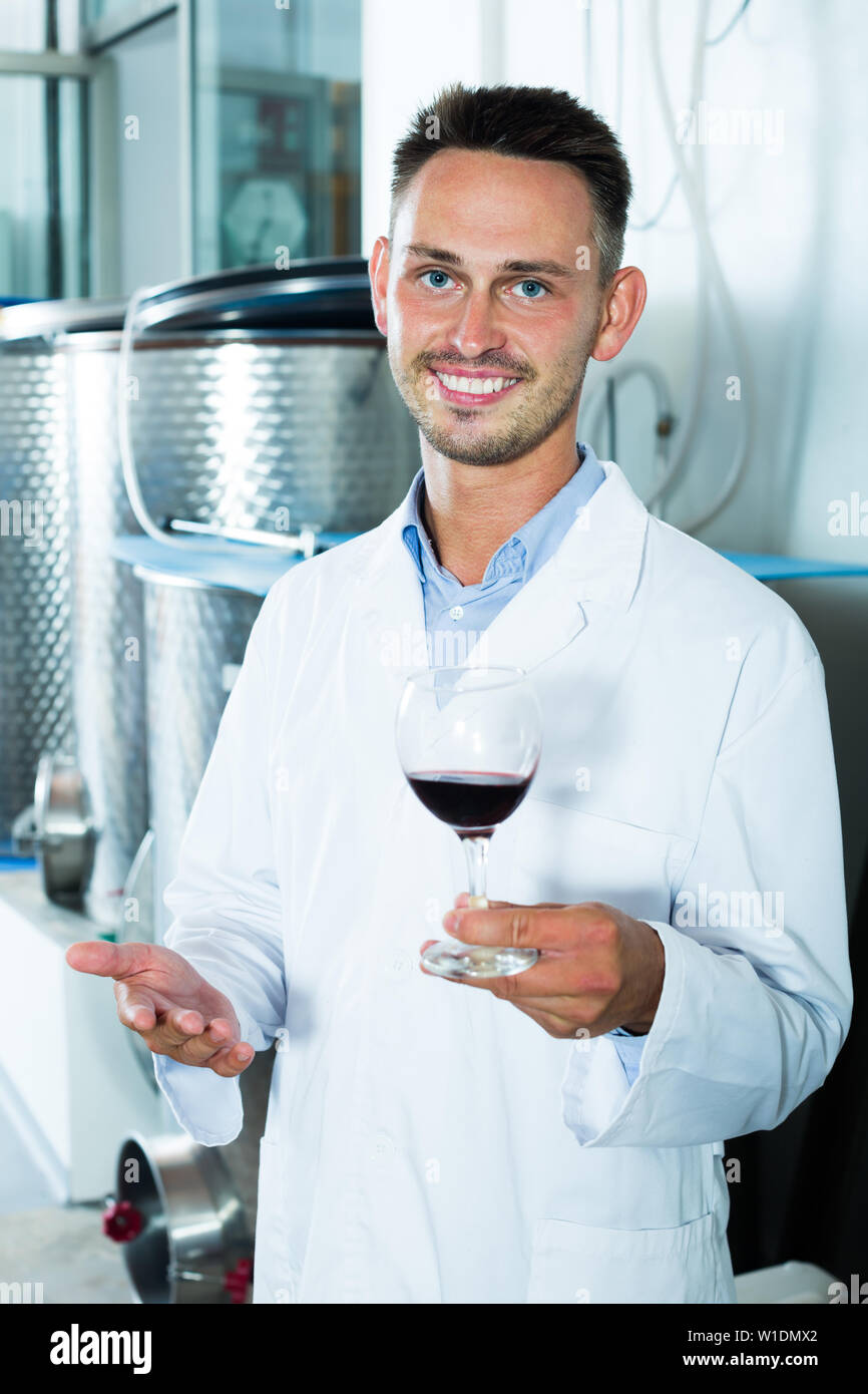 Glad winery worker wearing white coat holding glass of wine in ...