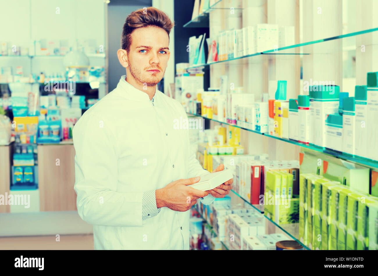 Smiling male pharmacist wearing white coat standing among shelves in ...