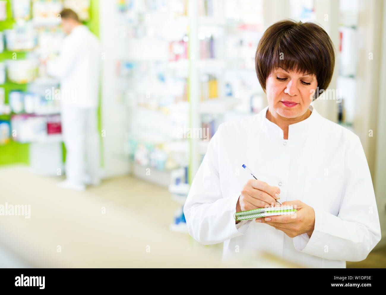 smiling woman pharmacist wearing uniform and working in pharmaceutical ...