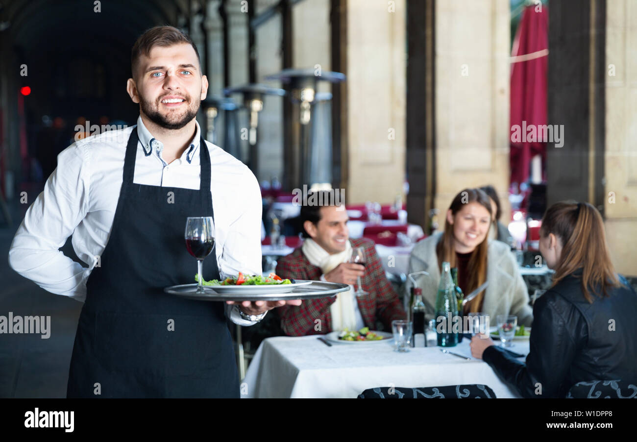 Portrait of glad cheerful positive waiter with serving tray meeting ...