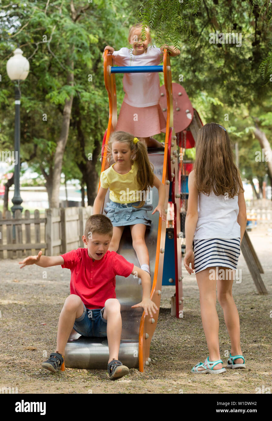 Cheerful boy and girl play games and running around sliding toy in park ...