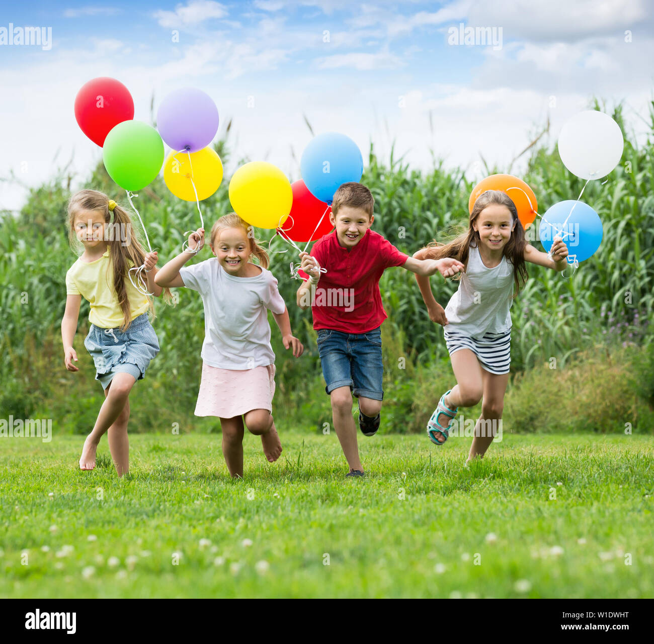 Four kids happily playing and running together on green lawn Stock ...