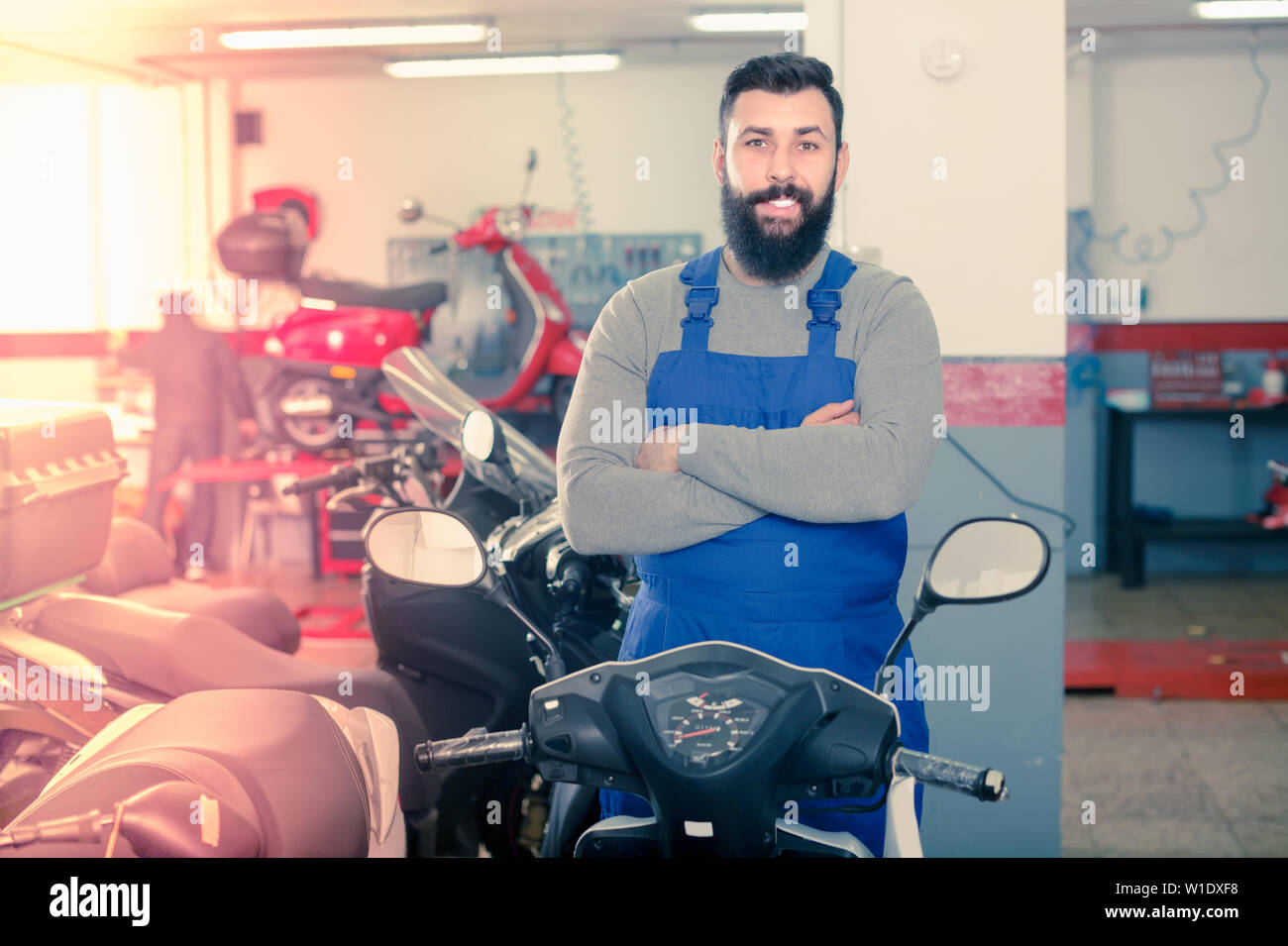Positive male worker showing motorbikes and scooters in motorcycle ...