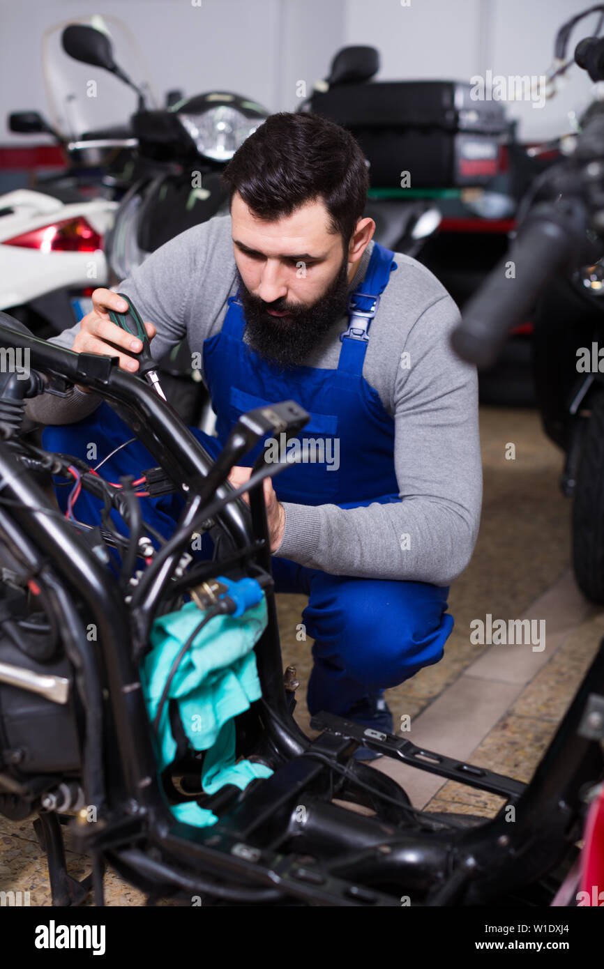 Young man worker working at restoring motorbike in motorcycle workshop ...