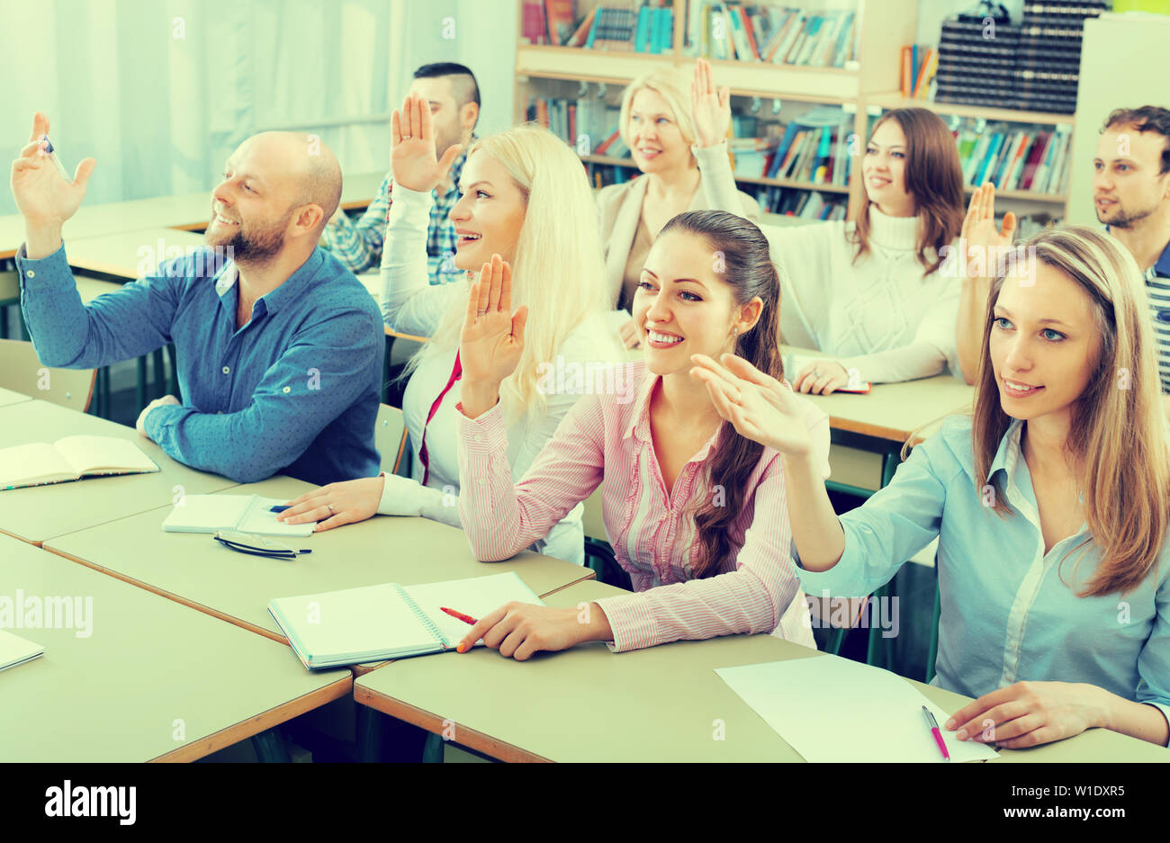 Positive adult students sitting in classroom with hands up. Focus on ...