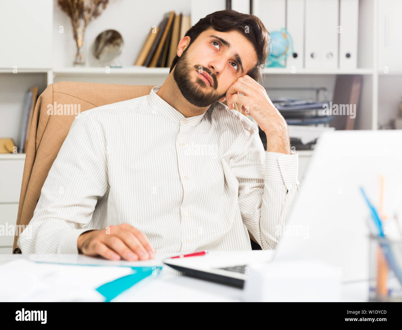 Portrait of handsome brunette manager having thoughtful look at office ...