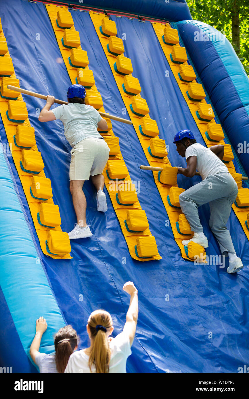 Two adult men having funny competition in climbing on inflatable castle ...