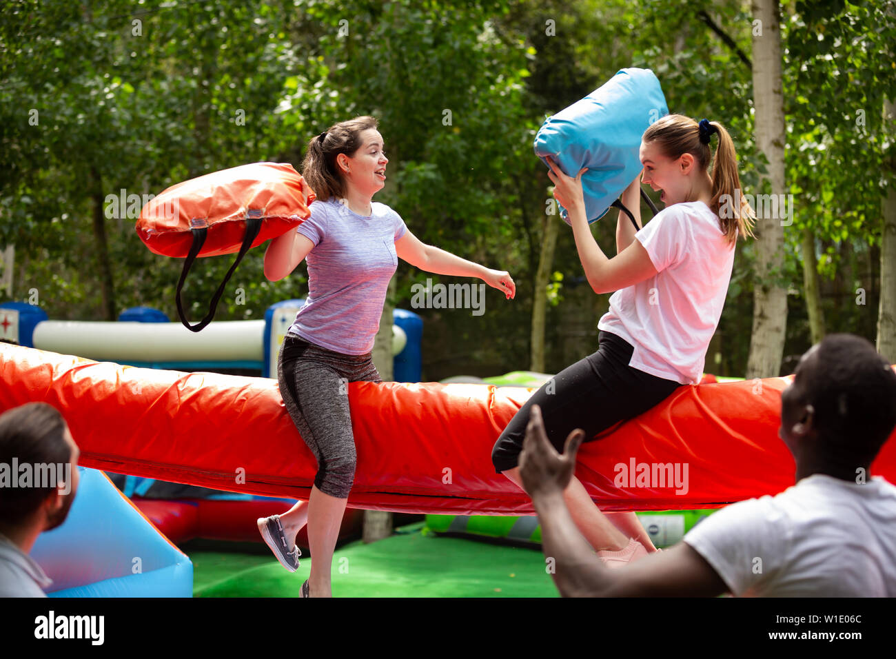 Laughing woman fighting by pillows with her female friend while sitting ...