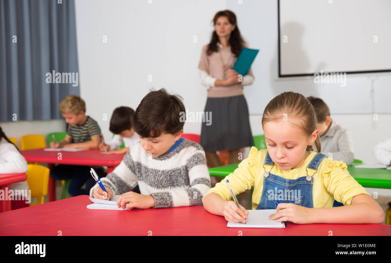 Portrait of diligent preteen students writing exercises at lessons with ...
